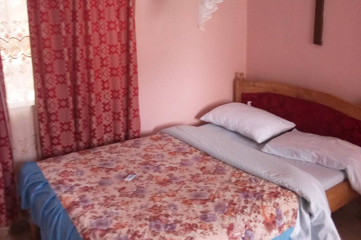 Quarto com cama, colcha florida, cortinas e mosquiteiro.