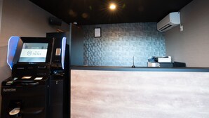 Uma área de recepção de hotel com um painel digital, um balcão de atendimento e um ar-condicionado fixado na parede.