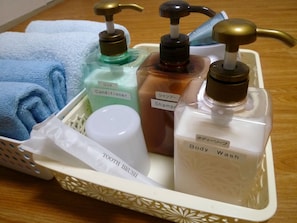 Área da pia do banheiro com produtos de higiene pessoal, incluindo gel de banho, shampoo, condicionador e escova de dentes.