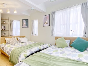 Quarto bem iluminado com duas camas, uma estante de livros e uma janela grande com cortinas.