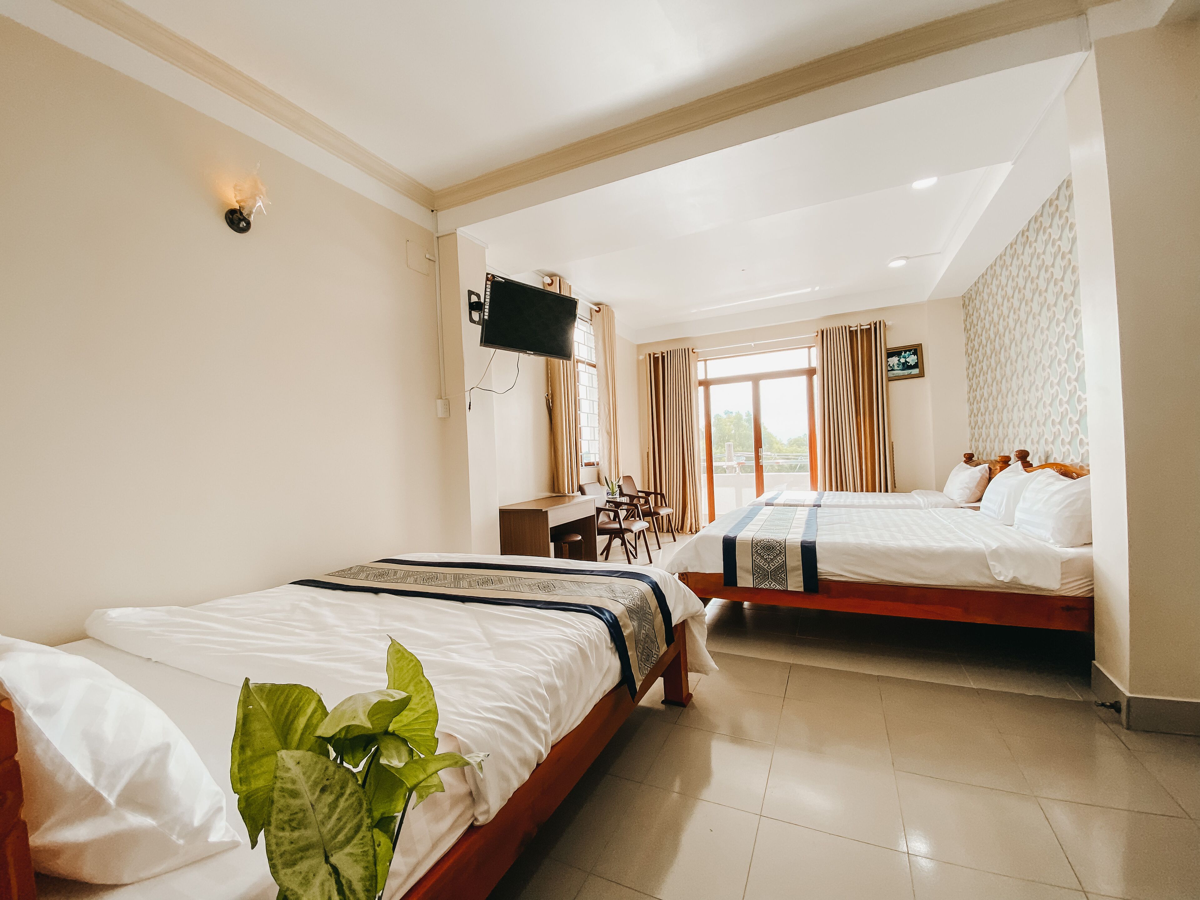 Quarto de hotel com duas camas, uma escrivaninha, uma televisão e uma janela grande com cortinas.