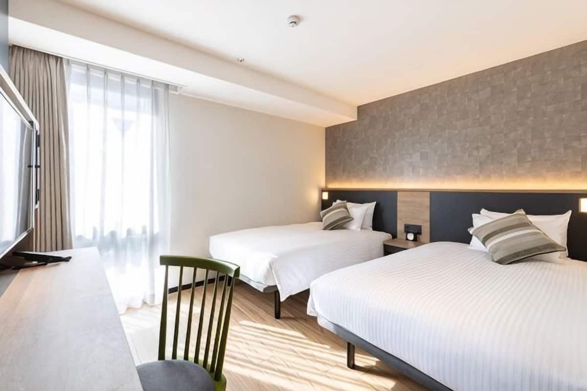 Quarto de hotel com duas camas, uma escrivaninha, uma cadeira e uma televisão.