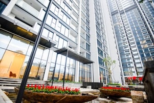Um edifício moderno com vários andares, grandes janelas e áreas de estar ao ar livre com flores vermelhas.