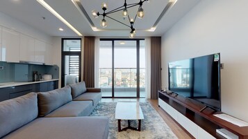 Uma sala de estar moderna com sofá, mesa de centro, televisão e vista da cidade através de grandes janelas.
