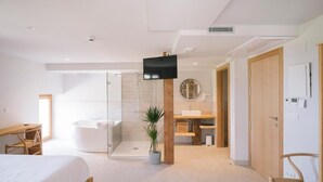 Quarto moderno com uma cama grande, chuveiro em box de vidro, televisão e banheiro com banheira e pia.