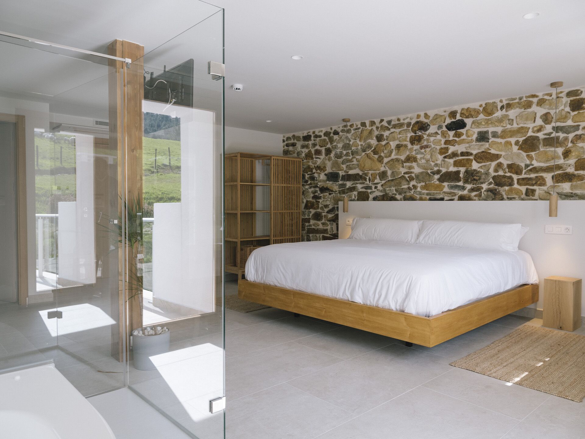 Quarto moderno com parede de pedra, box de chuveiro em vidro e estrutura de cama em madeira.