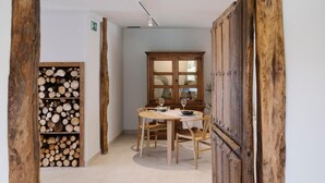 Uma área de jantar rústica de madeira, com mesa e cadeiras, um armário com portas de vidro e uma estante com lenha.