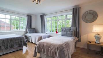 Quarto com duas camas, janelas amplas, mesa de cabeceira com abajur e espelho decorativo na parede.