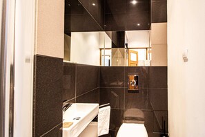 Uma casa de banho moderna com azulejos escuros, uma pia branca e um espelho.