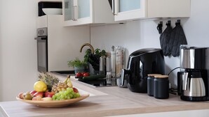 Cozinha moderna com armários brancos, cafeteira e uma fruteira no balcão.