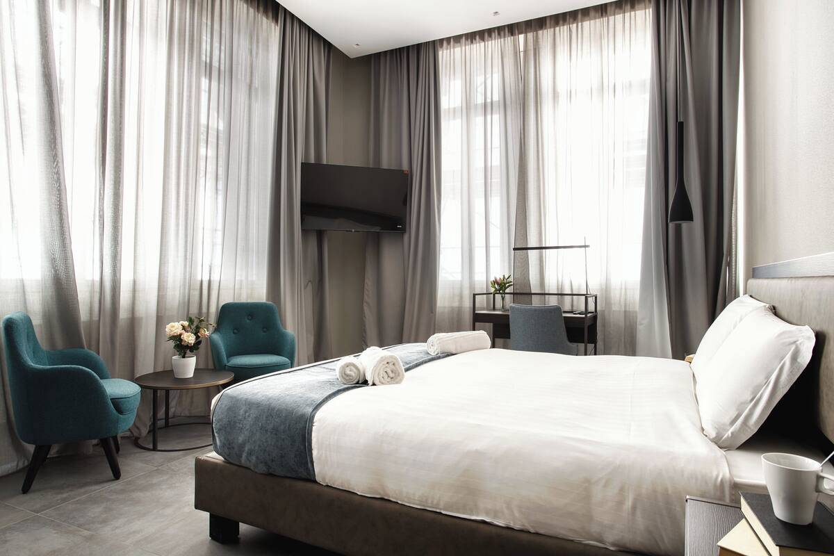 Quarto de hotel moderno com uma cama grande, televisão de tela plana, escrivaninha com cadeira e um sofá.