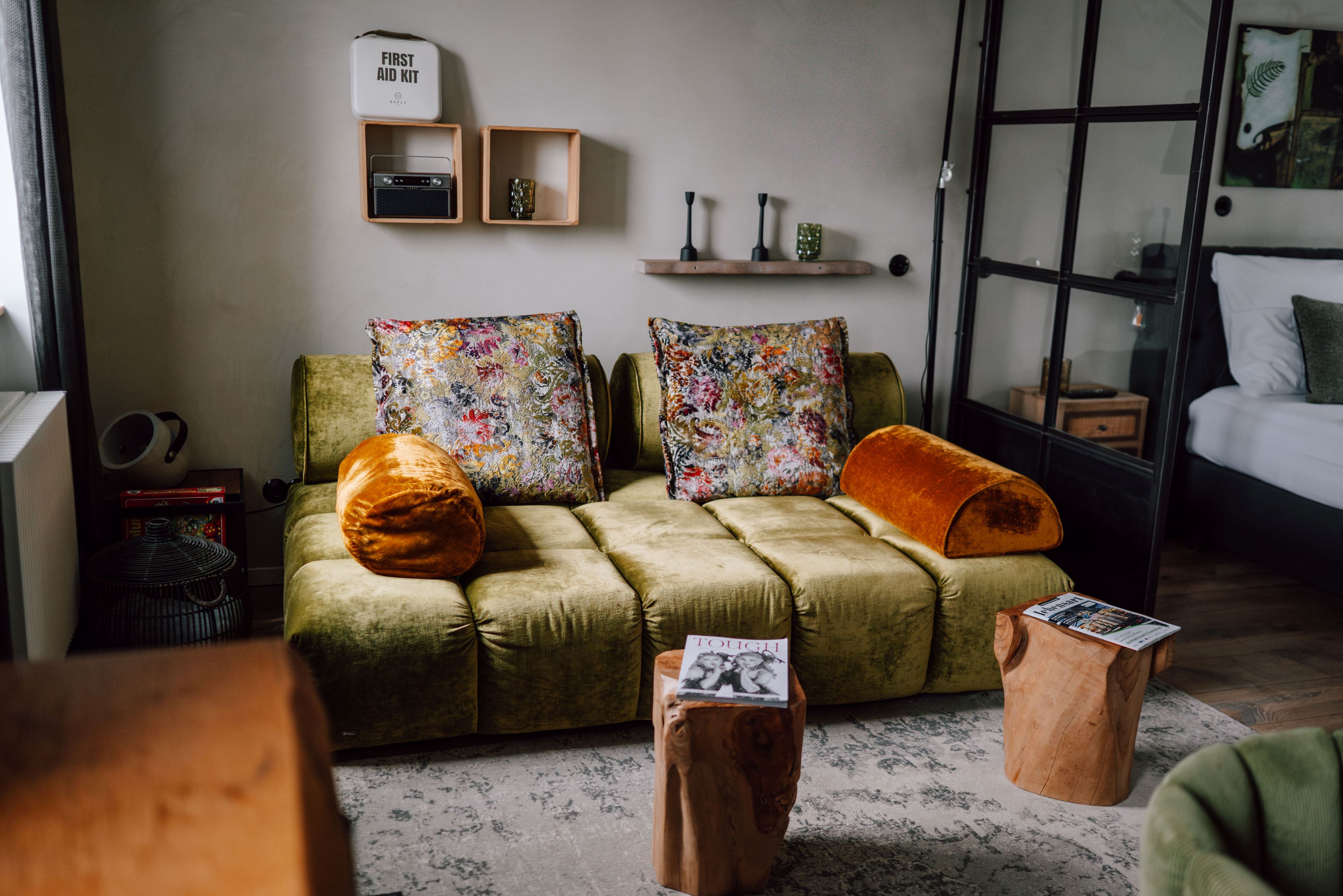 Uma sala de estar acolhedora com um sofá verde, duas almofadas decorativas, uma pequena mesa de madeira e uma prateleira com um kit de primeiros socorros.