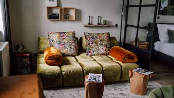 Uma sala de estar acolhedora com um sofá verde, duas almofadas decorativas, uma pequena mesa de madeira e uma prateleira com um kit de primeiros socorros.