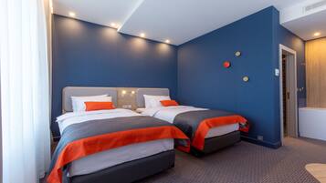 Quarto de hotel com duas camas, uma porta de madeira e uma mesa pequena.