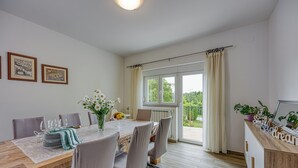 Uma sala de jantar com uma mesa de madeira, cadeiras e vista para o exterior.