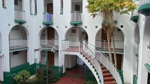 Um pátio com uma escadaria central, rodeado por edifícios brancos com detalhes verdes e varandas.
