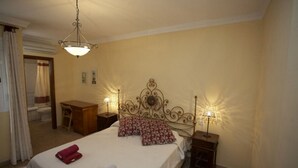 Um quarto com cama, luminárias de cabeceira, uma escrivaninha e uma cadeira.
