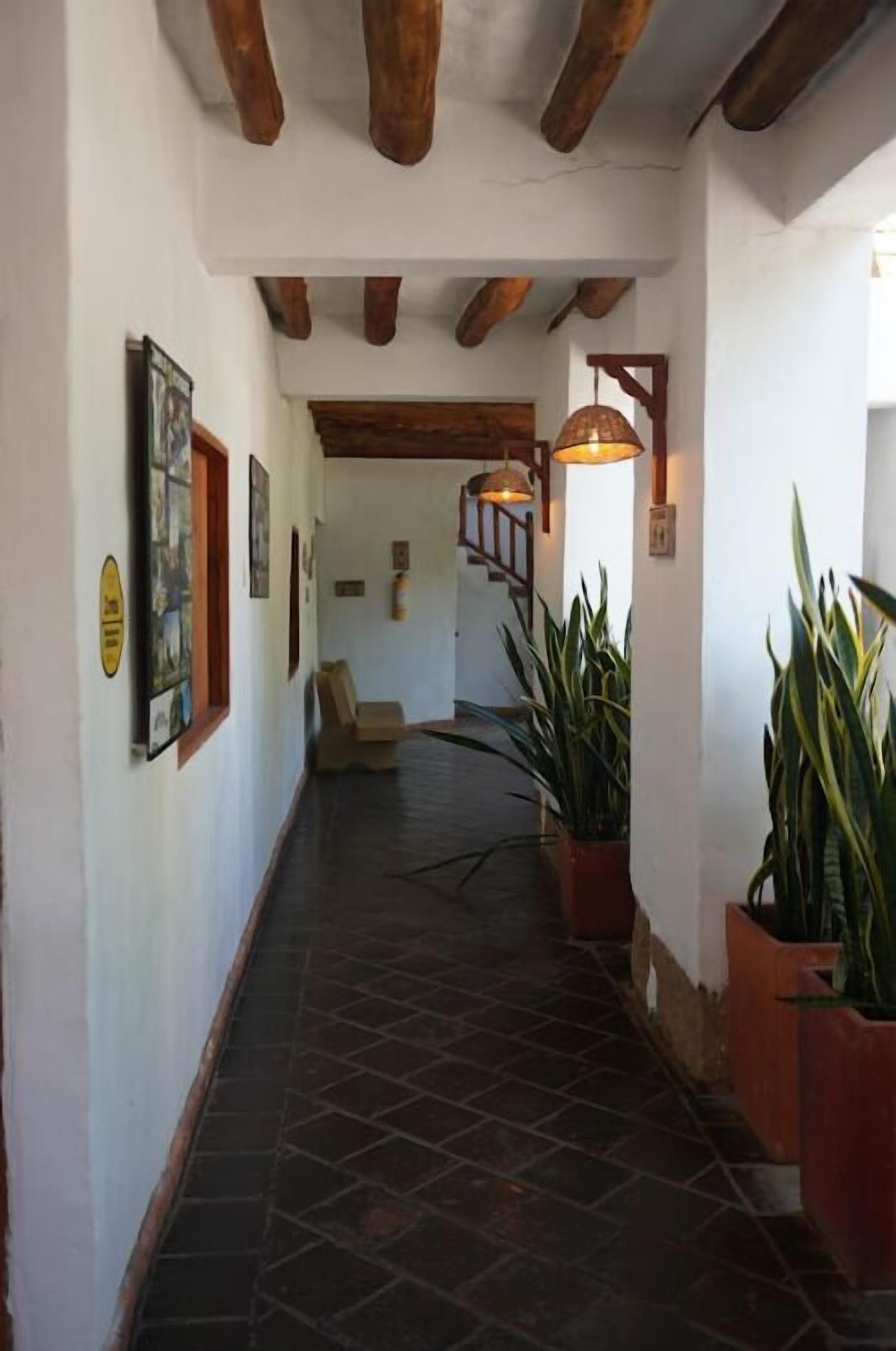 Um corredor com vigas de madeira, soalho em azulejos e plantas em vasos.
