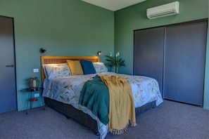 Quarto com cama, mesa de cabeceira, abajur e aparelho de ar condicionado.