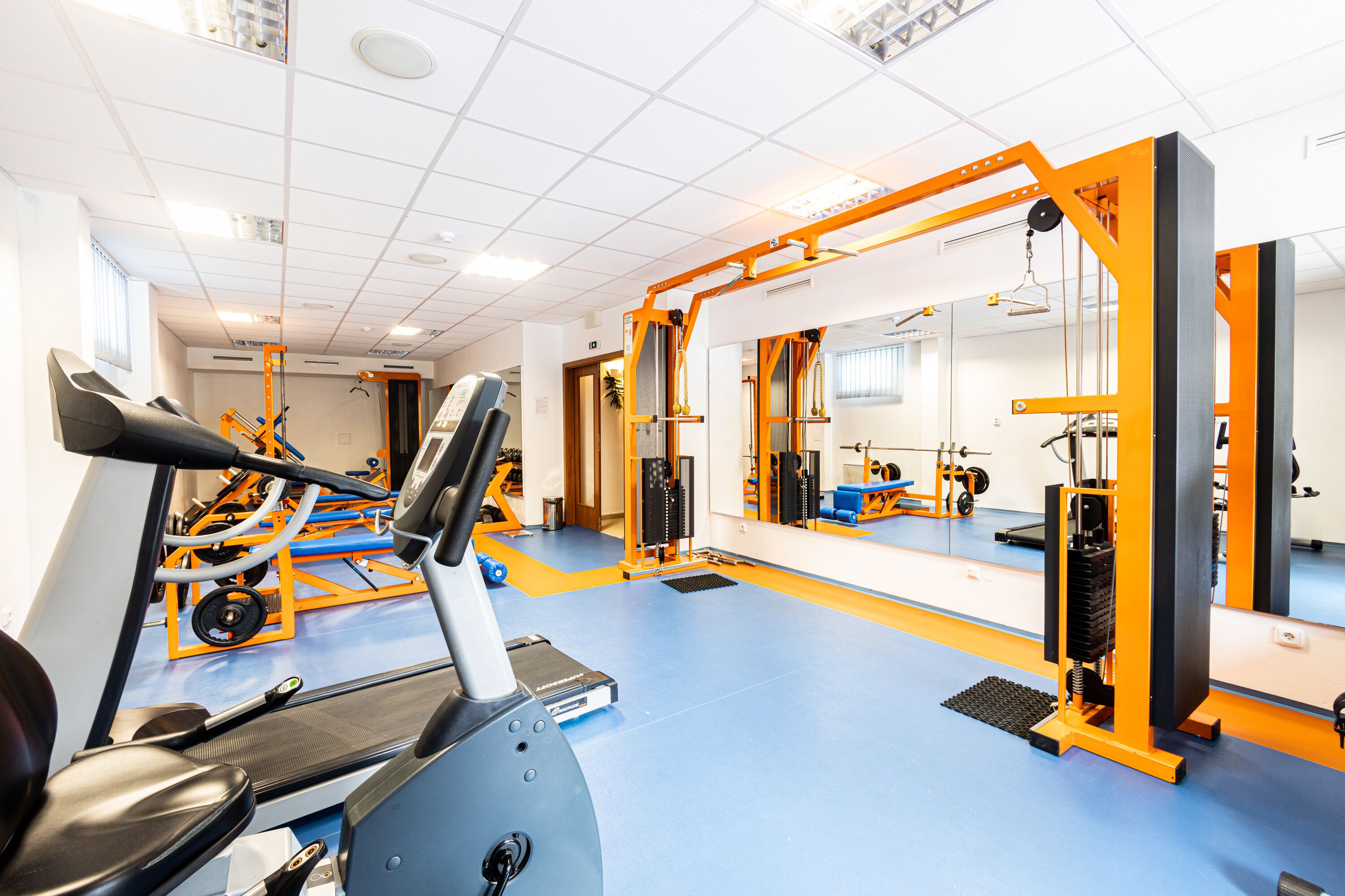Uma academia com equipamentos de ginástica, um espelho e piso azul.