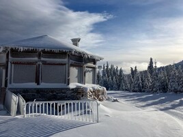 Um edifício coberto de neve, com alicerce de pedra e uma vedação de metal à frente.