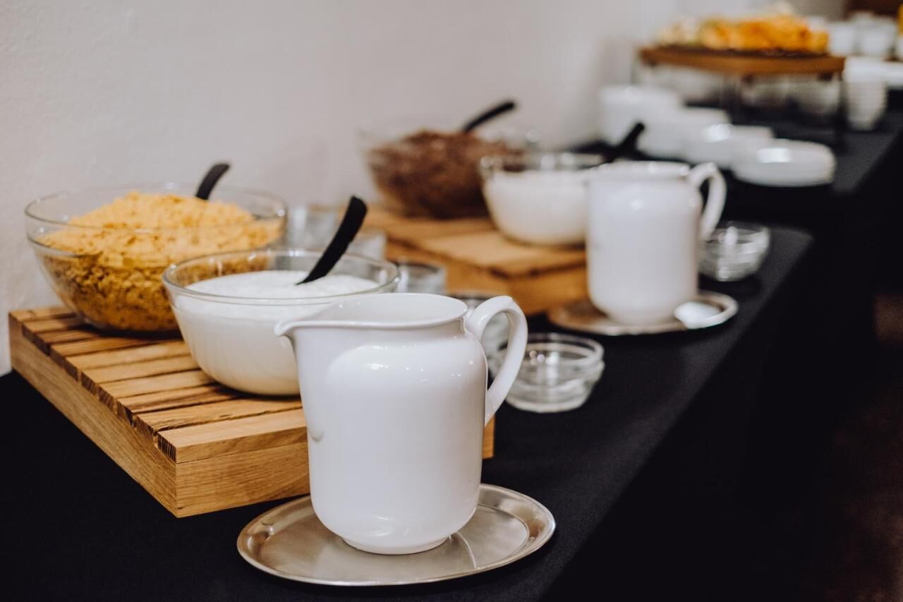 Disposição de buffet com tigelas de cereais e leite, e um jarro sobre uma tábua de madeira.