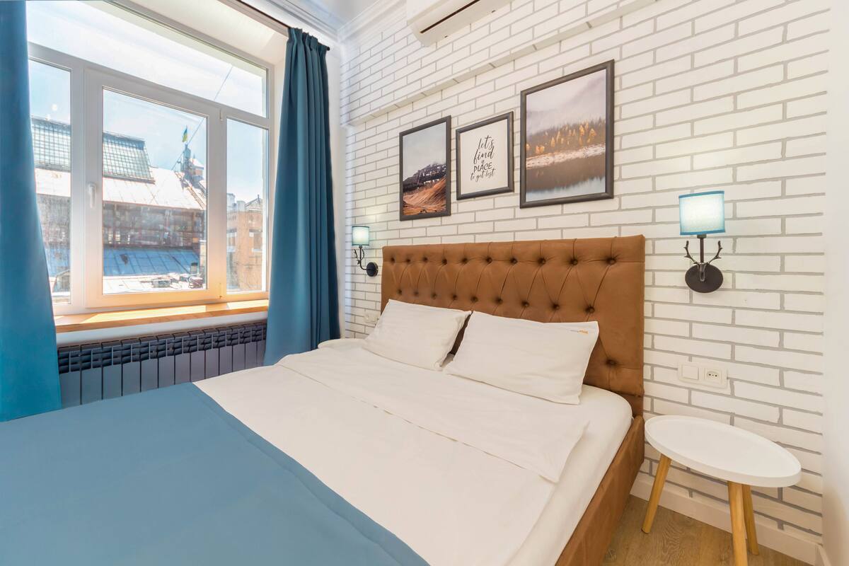 Quarto de hotel com uma cama grande, uma pequena mesa redonda e vista para um edifício pela janela.