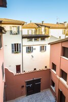 Um estreito beco entre edifícios com telhados e persianas, uma entrada gradeada e uma pequena área externa com piso estampado.