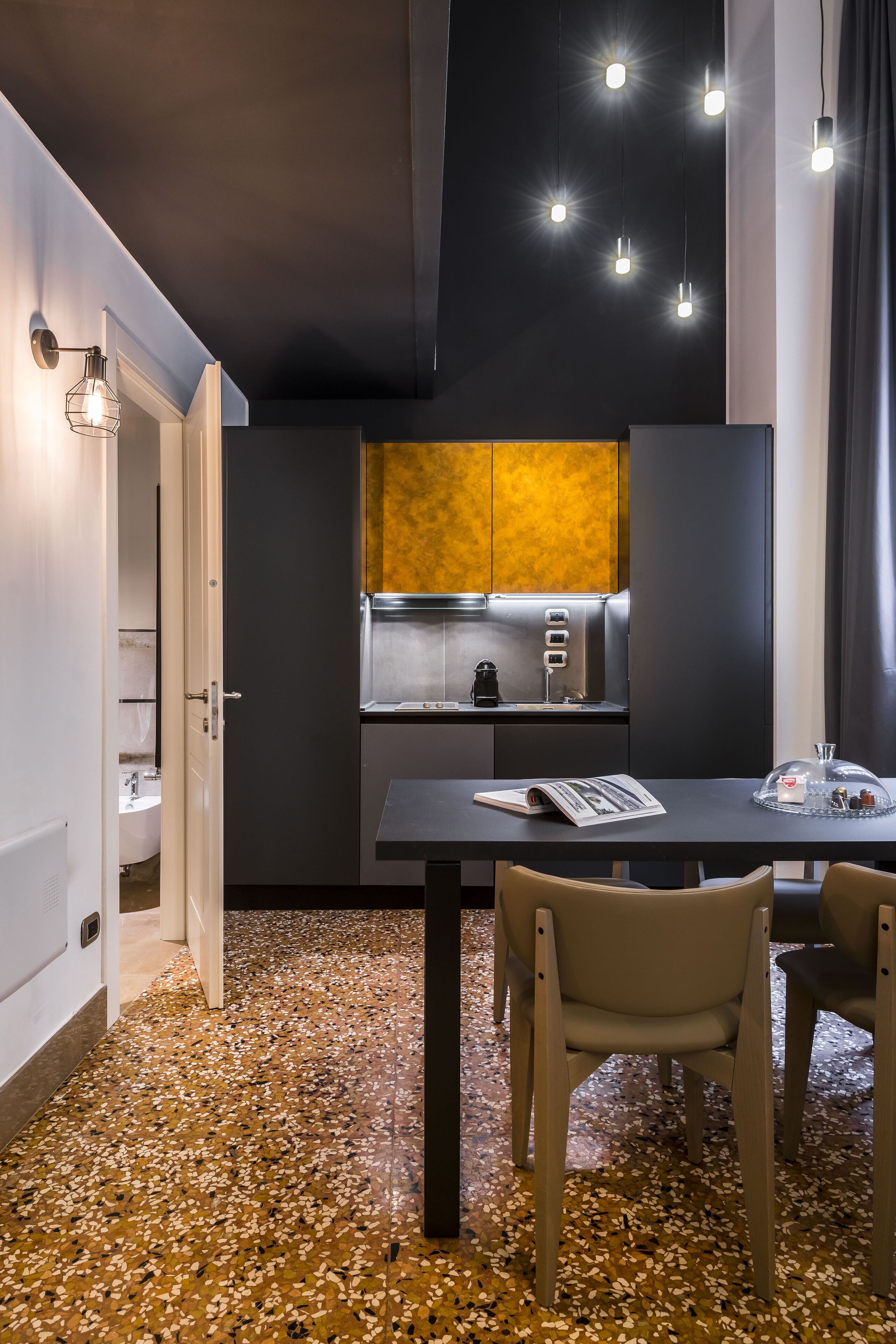Cozinha moderna com teto escuro, painel de parede amarelo e área de refeições com duas cadeiras e uma mesa.