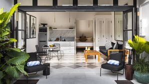 Uma sala de estar moderna com piso xadrez, móveis preto e branco e plantas verdes grandes.