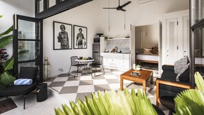 Uma sala de estar moderna com piso xadrez, uma área de jantar com mesa redonda e uma cozinha com armários brancos.