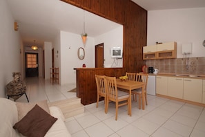 Uma sala de estar com uma mesa de jantar de madeira, cadeiras, um sofá e uma TV no canto.