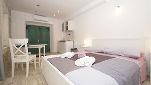 Quarto com cama, uma cadeira, uma mesa e porta verde.