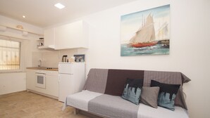 Um espaço compacto com cozinha compacta, um sofá com almofadas e um quadro de um veleiro na parede.