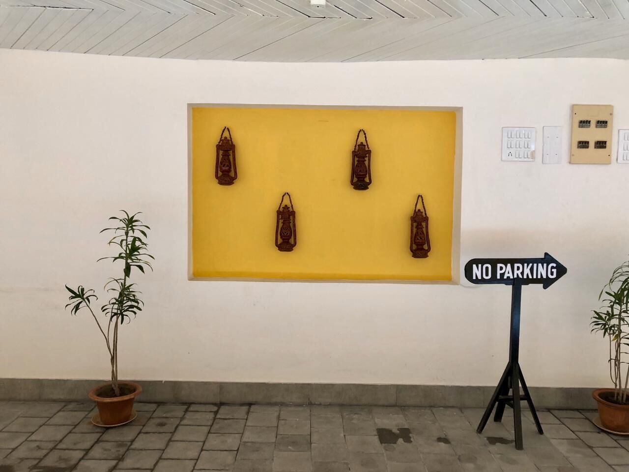 Um corredor com parede amarela, placa de 'NÃO ESTACIONAR' e plantas em vasos.