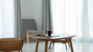Quarto moderno e minimalista com uma mesa redonda de madeira, uma cadeira de vime e um poltrona cinza.