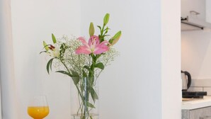 Quarto moderno com mesa de consola de madeira, uma cadeira branca, um vaso com flores e um copo de sumo de laranja.