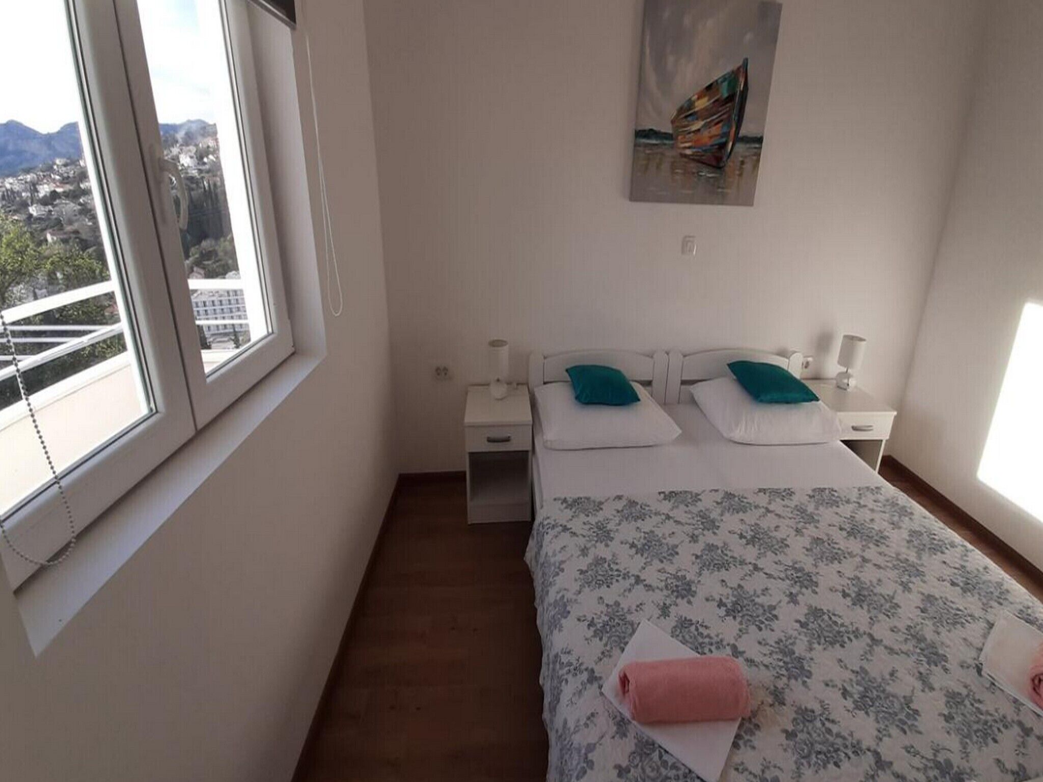 Quarto com cama, duas mesas de cabeceira, uma janela e um quadro na parede.
