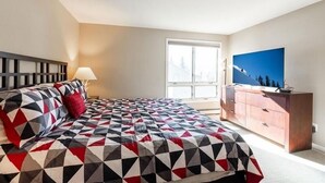 Quarto com cama, cômoda, televisão e janela.