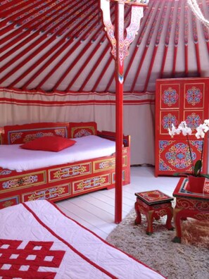 Quarto no estilo tradicional mongol, com uma cama, uma mesa pequena e um armário decorativo.