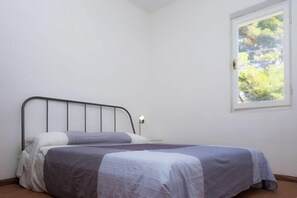 Cama individual com estrutura de metal e janela com vista para árvores.