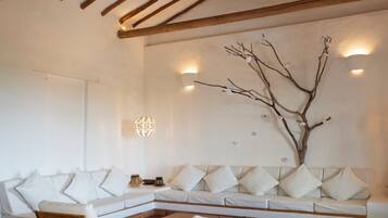 Uma sala de estar aconchegante com teto de madeira, um sofá branco com almofadas, uma mesa de centro de madeira e piso de tijolos.