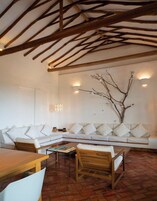 Uma sala de estar aconchegante com teto de madeira, um sofá branco com almofadas, uma mesa de centro de madeira e piso de tijolos.