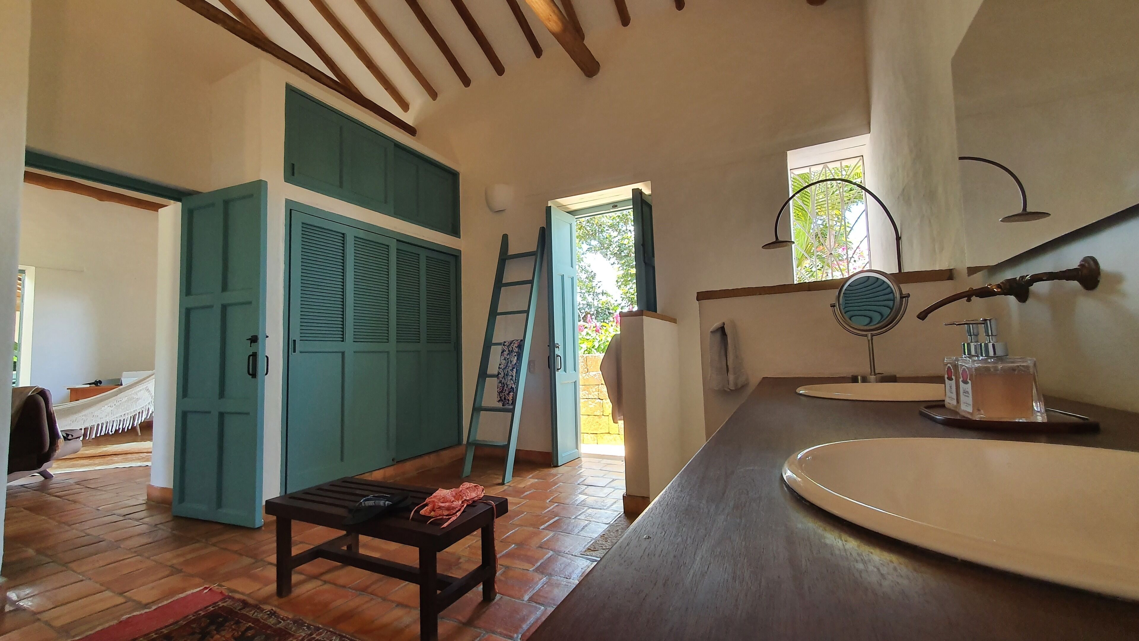 Casa de banho com lavatório, espelho e barra de toalhas. Há um banco de madeira e uma escada na divisão.