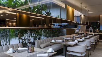 Um restaurante moderno com mesas altas, cabines, amplas janelas e plantas em interior.