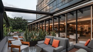 Uma área externa moderna com sofás e cadeiras, um espaço envidraçado e vista para o interior do edifício.