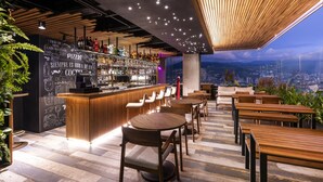 Uma área de bar moderna com teto de madeira, banquetas e vista para a cidade.