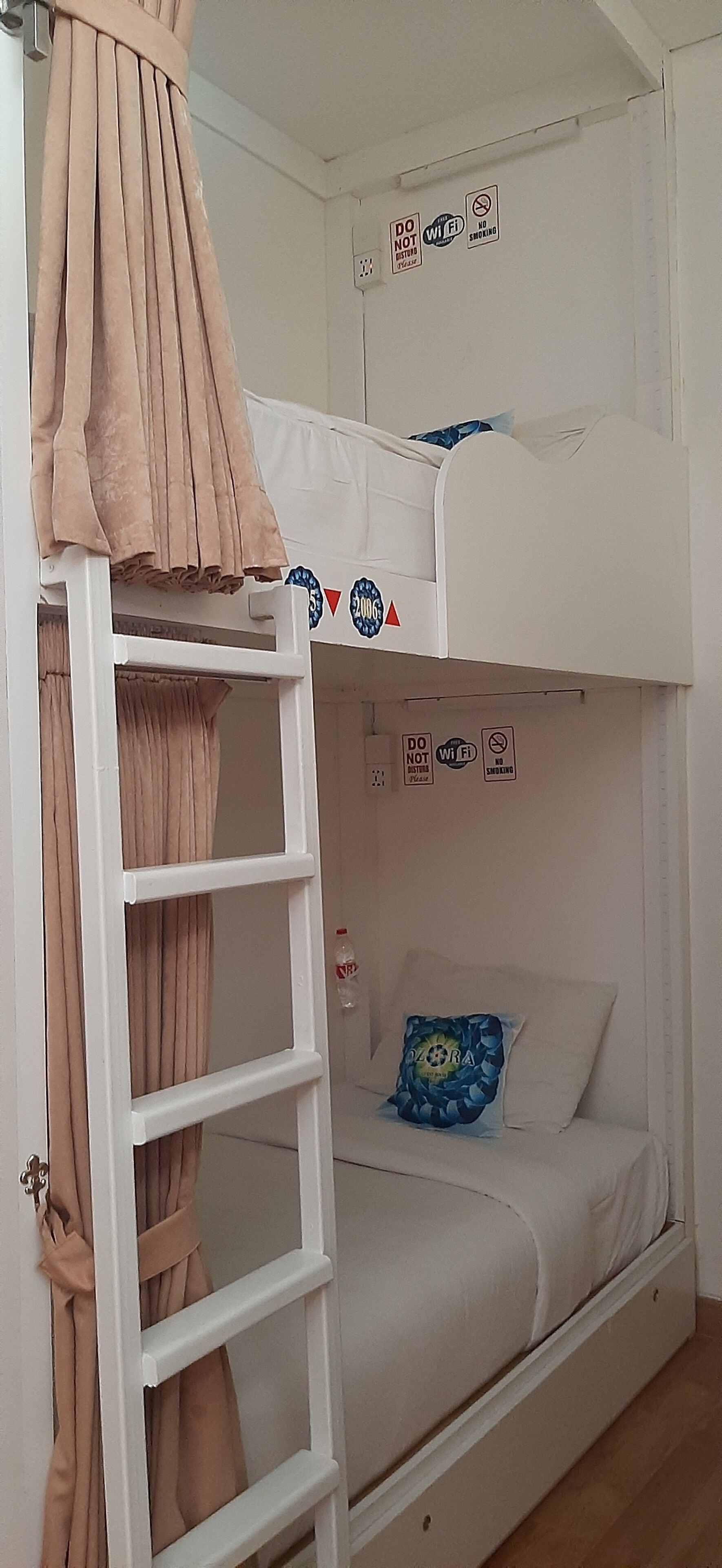 Uma cama beliche com escada, um travesseiro com logótipo e uma cortina.
