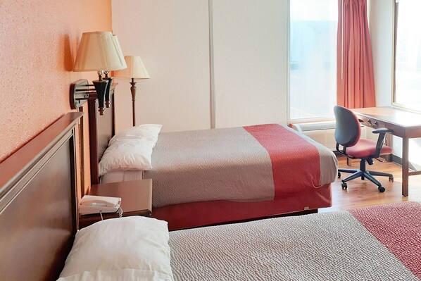 Quarto de hotel com cama, mesa de cabeceira, abajur, escrivaninha, cadeira e vista da cidade pela janela.