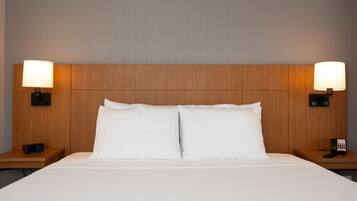 Quarto de hotel com uma cama grande, duas mesas de cabeceira, um painel de cama de madeira e duas luminárias fixadas na parede.